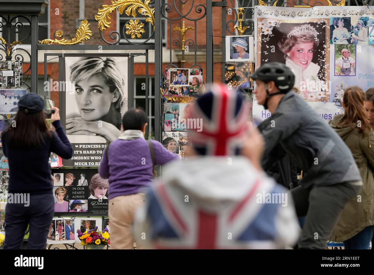 People stand in front of pictures of Princess Diana at the gates of ...