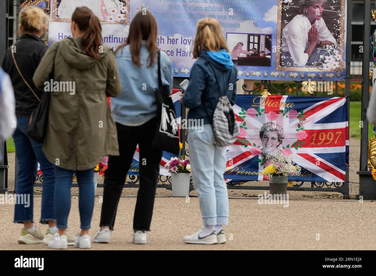 People stand in front of pictures of Princess Diana at the gates of ...