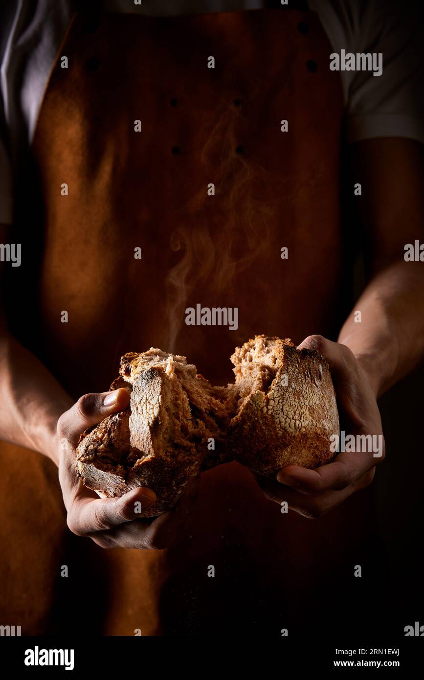 Bread in the hands of a professional baker. Dark background. Breaking ...