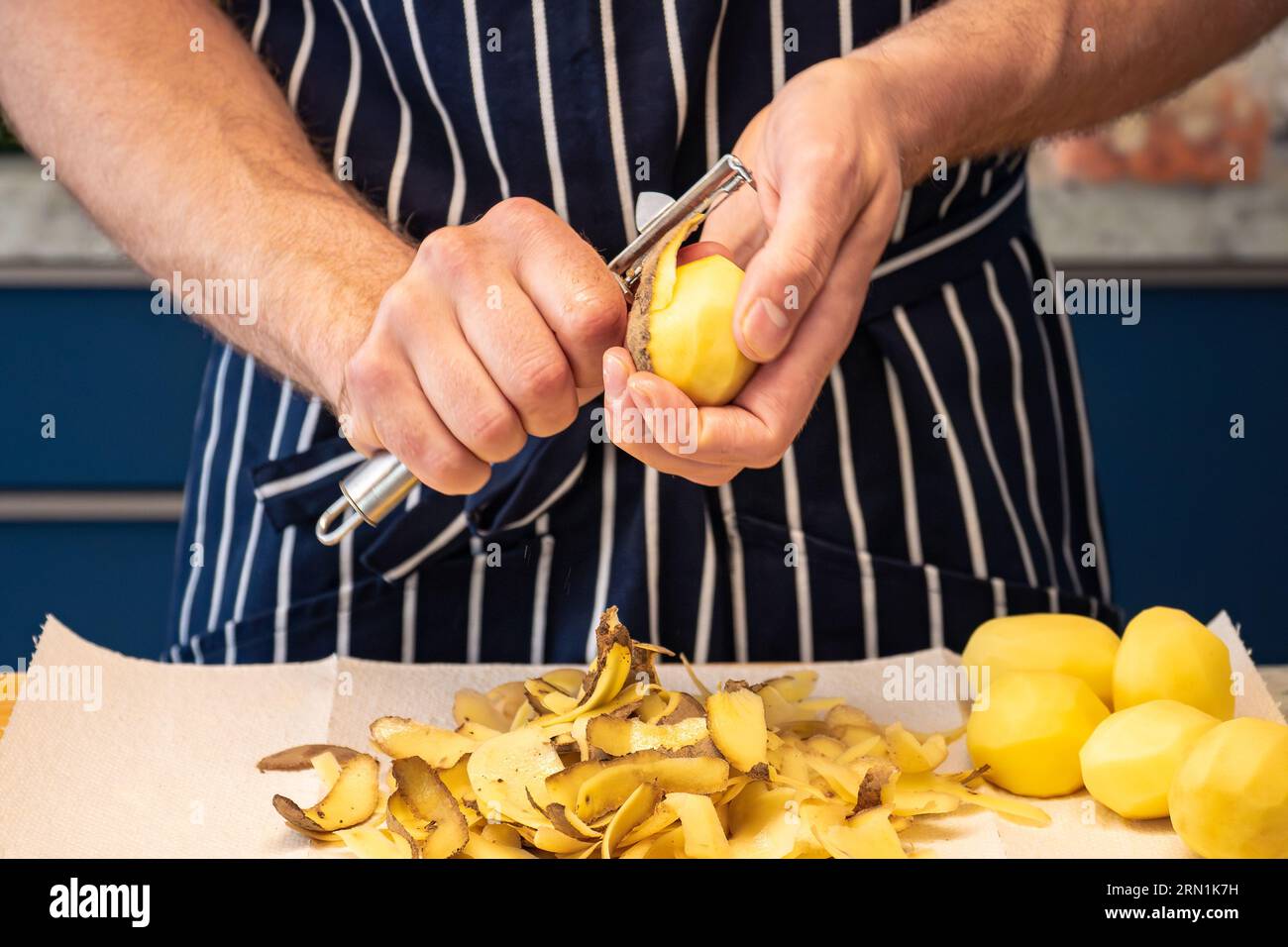 male chef hands peeling a bunch of potatoes with a food peeler in front ...