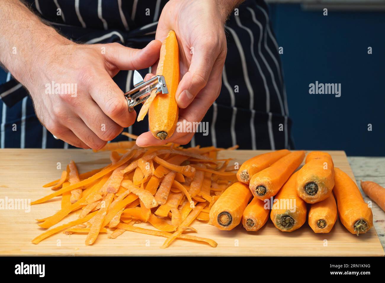 male chef hands peeling a bunch of carrots with a food peeler in front ...