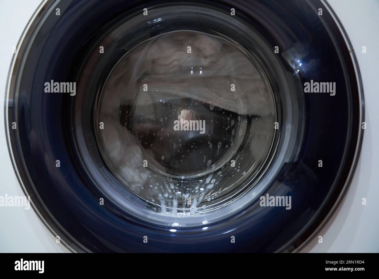 Wet white laundry in the drum of the washing machine. Close-up glass ...