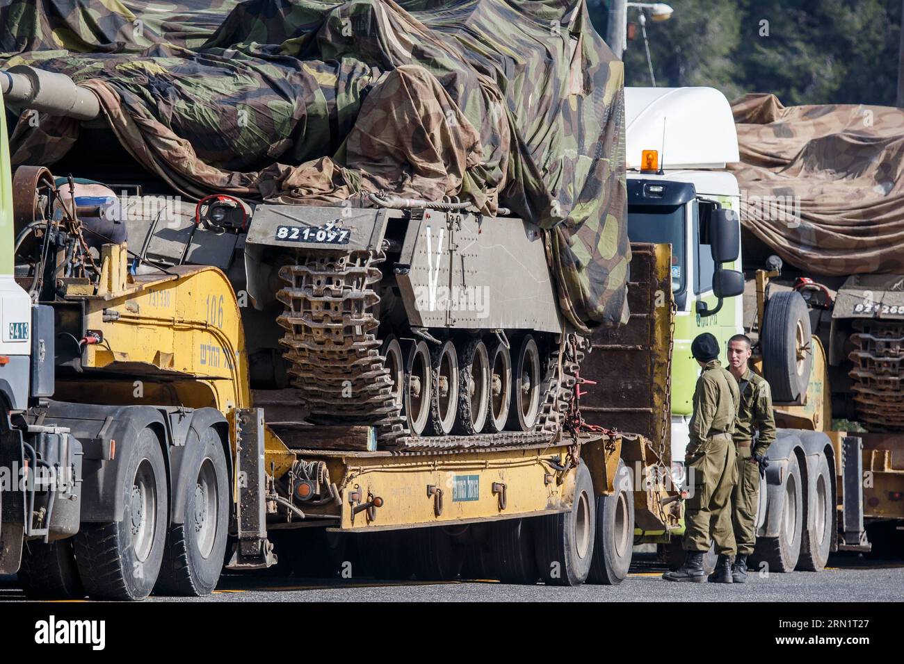 Israeli soldiers stand next to trucks carrying tanks near the border ...