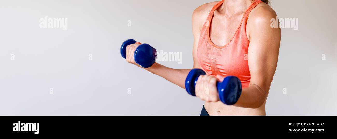 Sporty female wearing sports bra doing gym exercise using dumbbells ...