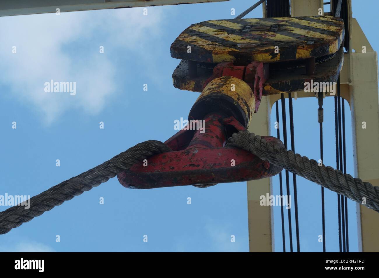 View on the red steel hook of ship's cargo crane secured by rope on ...