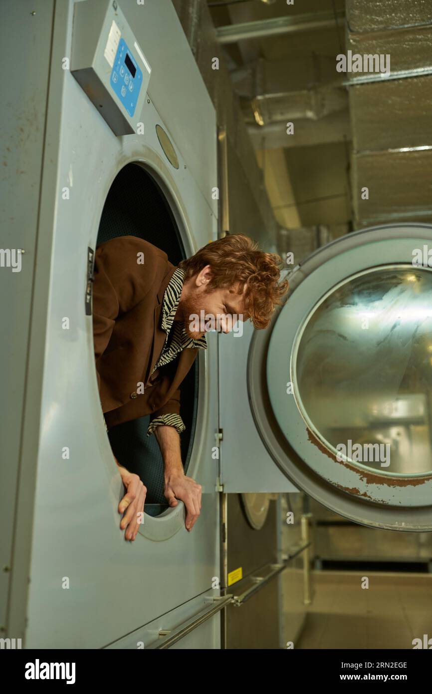 cheerful and trendy young redhead man posing in washing machine in ...