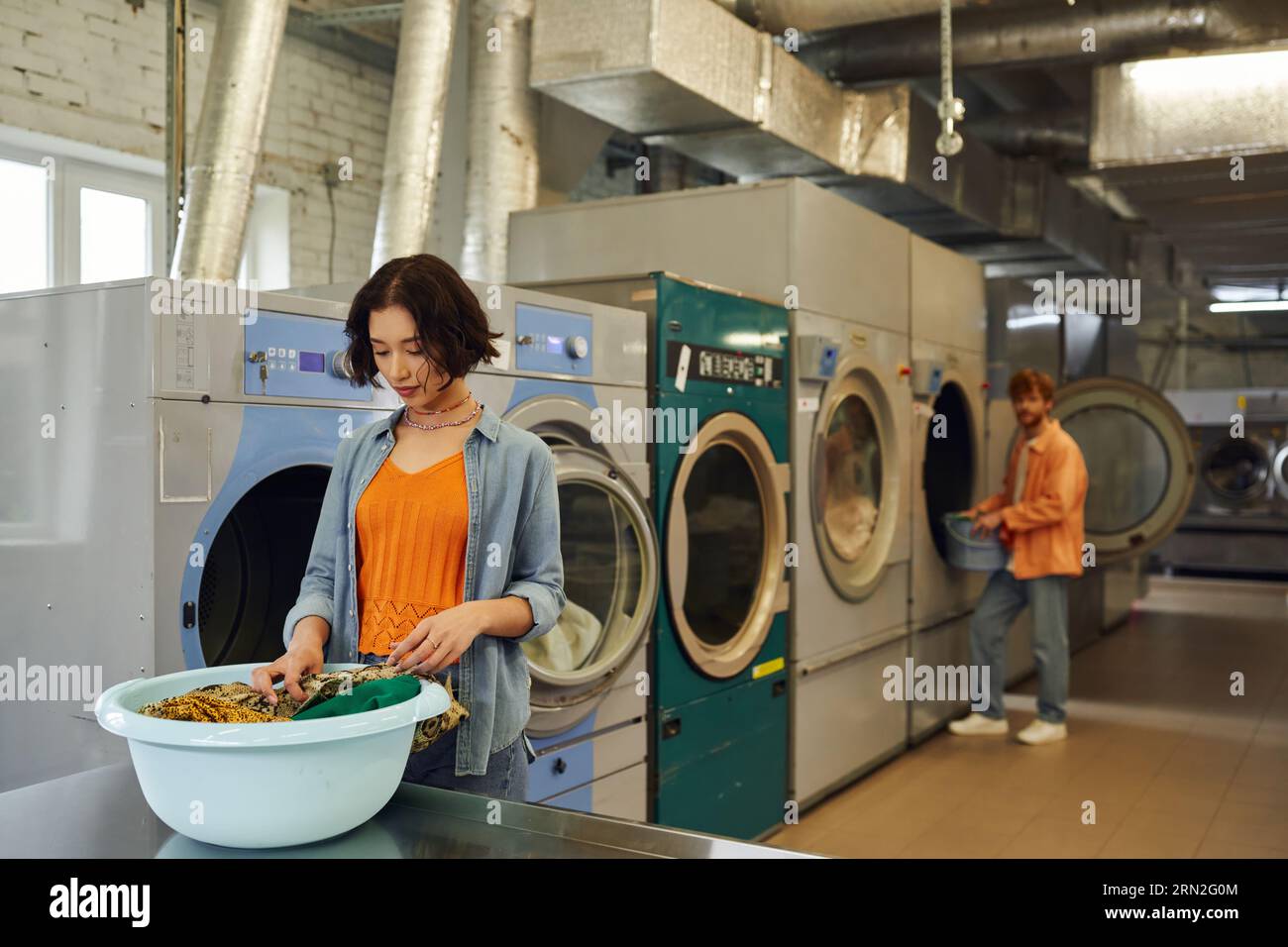 young asian woman sorting clothes in basin near blurred boyfriend in public laundry Stock Photo ...
