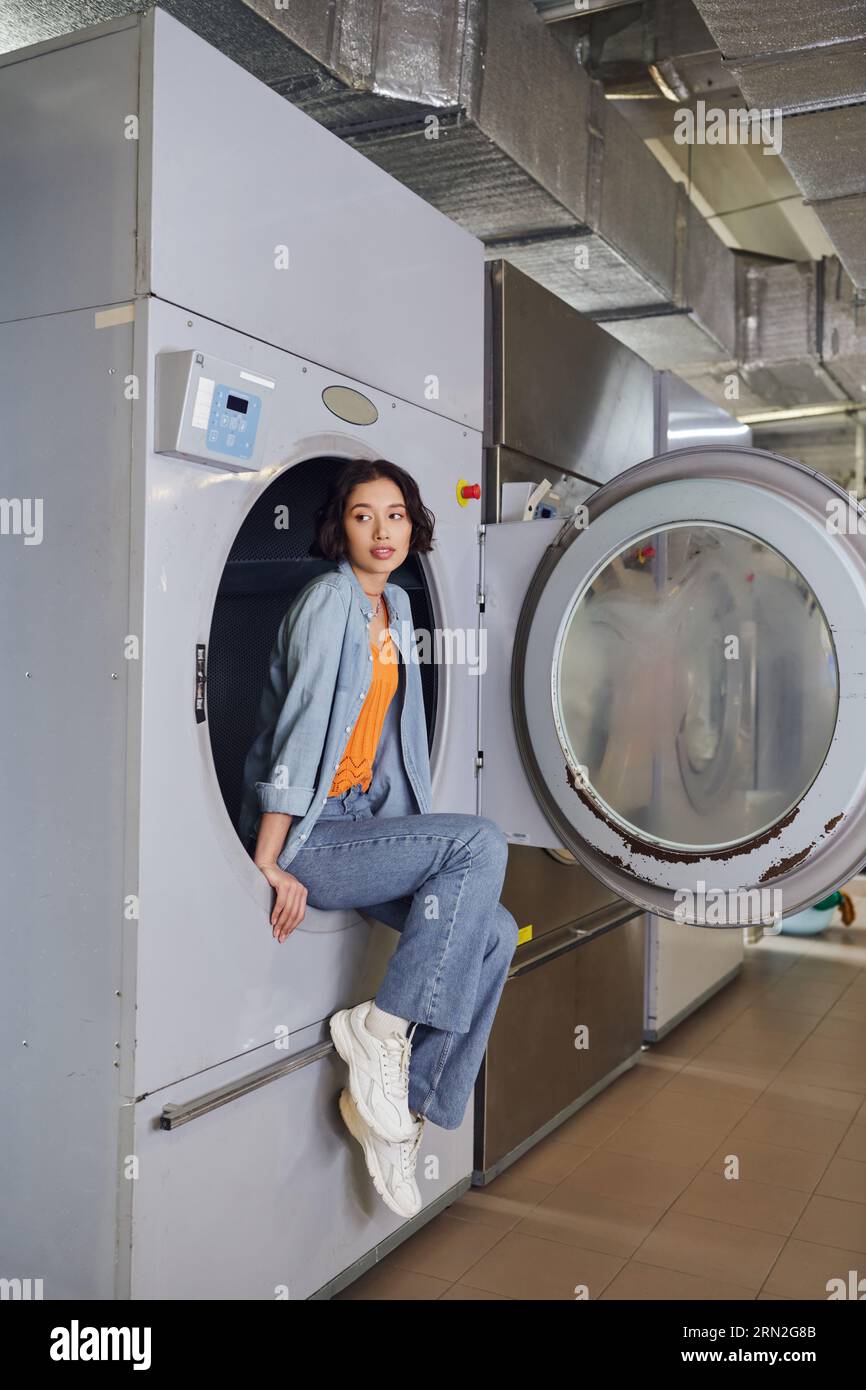 full length of young asian woman sitting on washing machine in public laundry Stock Photo - Alamy