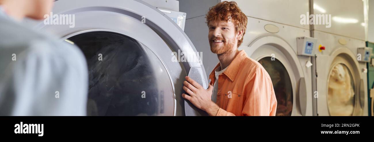 smiling young man standing near washing machines and girlfriend in self ...