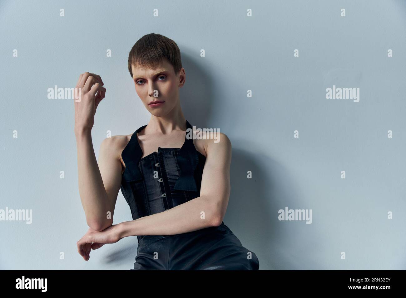androgynous model in black corset posing on grey backdrop, queer ...