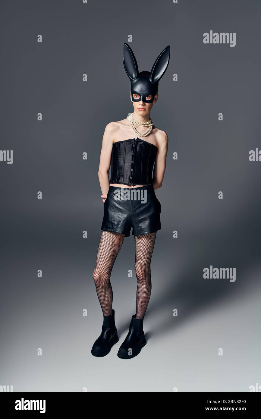 androgynous model in black corset posing in bdsm bunny mask on grey ...