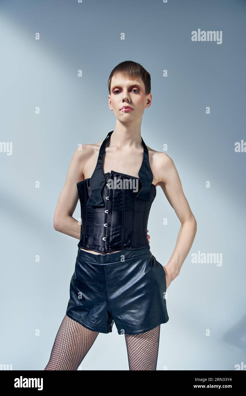 queer model in black corset and shorts posing on grey backdrop ...