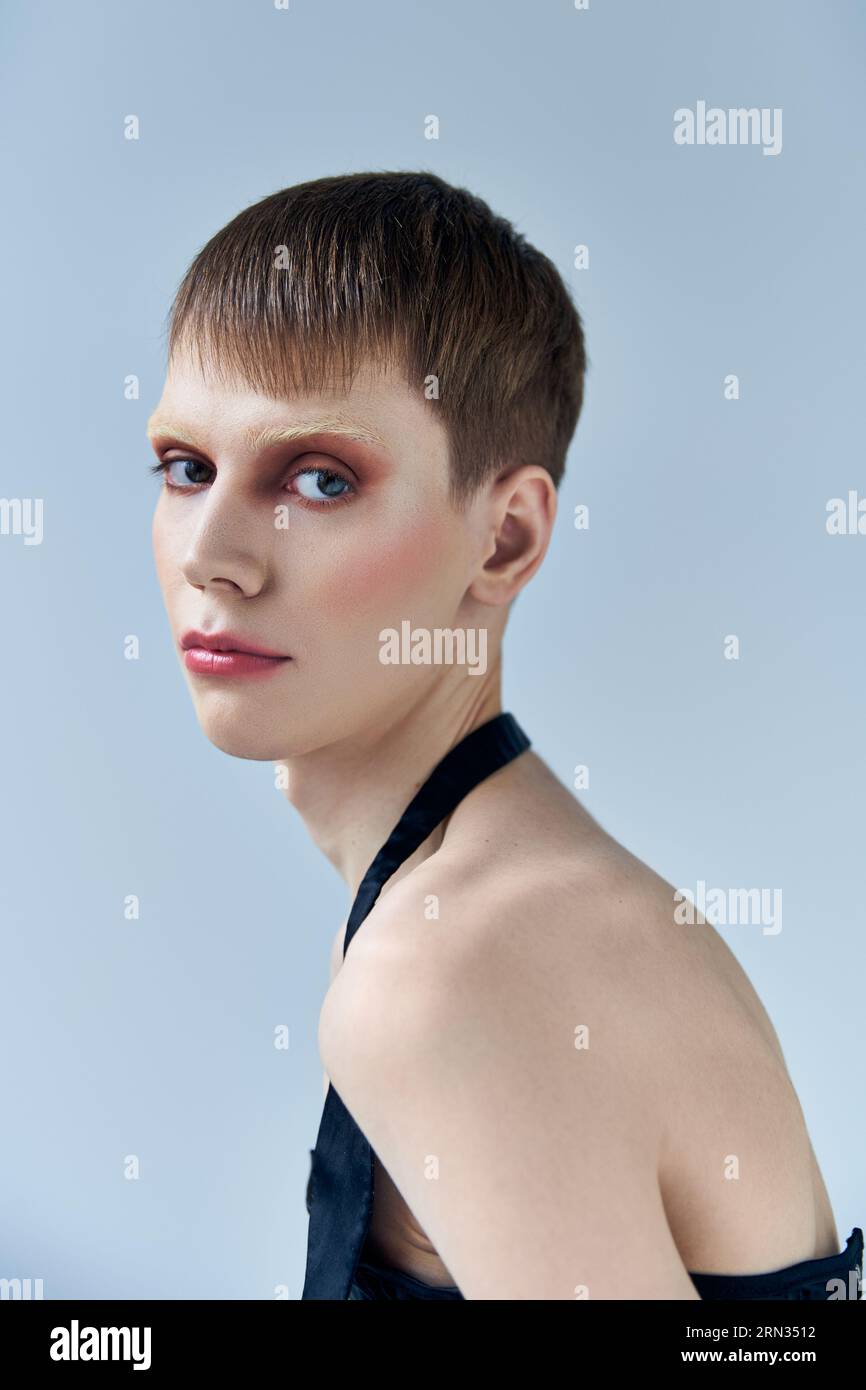 androgynous model with makeup looking at camera, grey backdrop, beauty ...