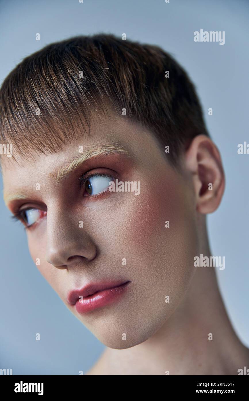queer person with makeup looking away, grey background, beauty and ...