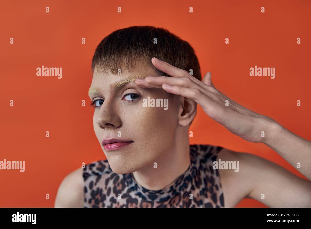 androgynous person smiling and looking at camera on orange backdrop ...