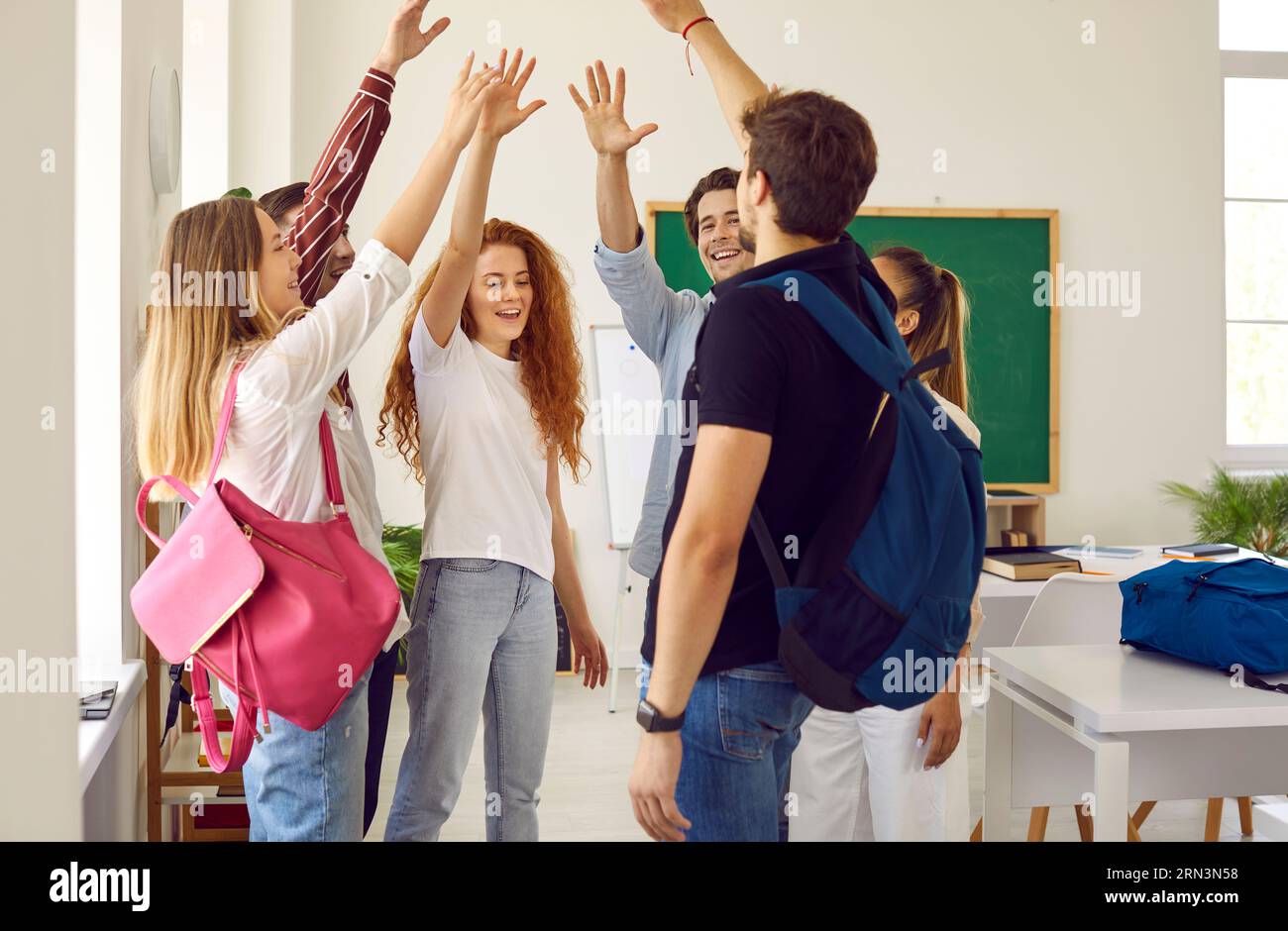 Team of happy students standing in the school classroom and giving each ...