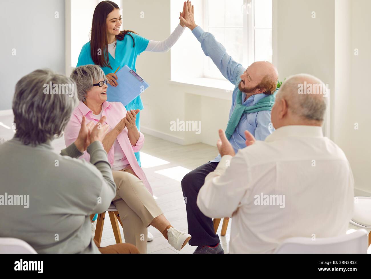Seniors doing high five in a group therapy session with a young nurse ...