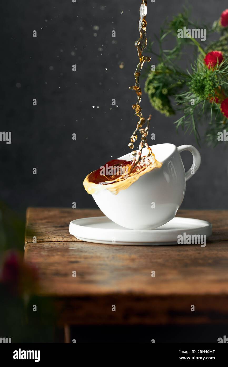 Artistic image of pouring black tea in a cup. Tea is splashing around ...