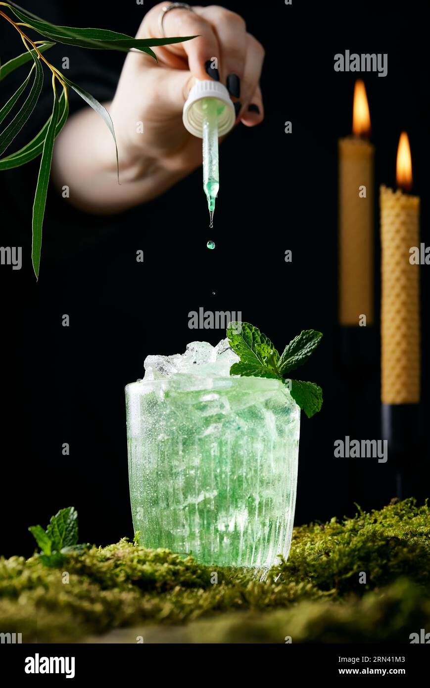Cropped hand dripping drops into very icy light green cocktail ...