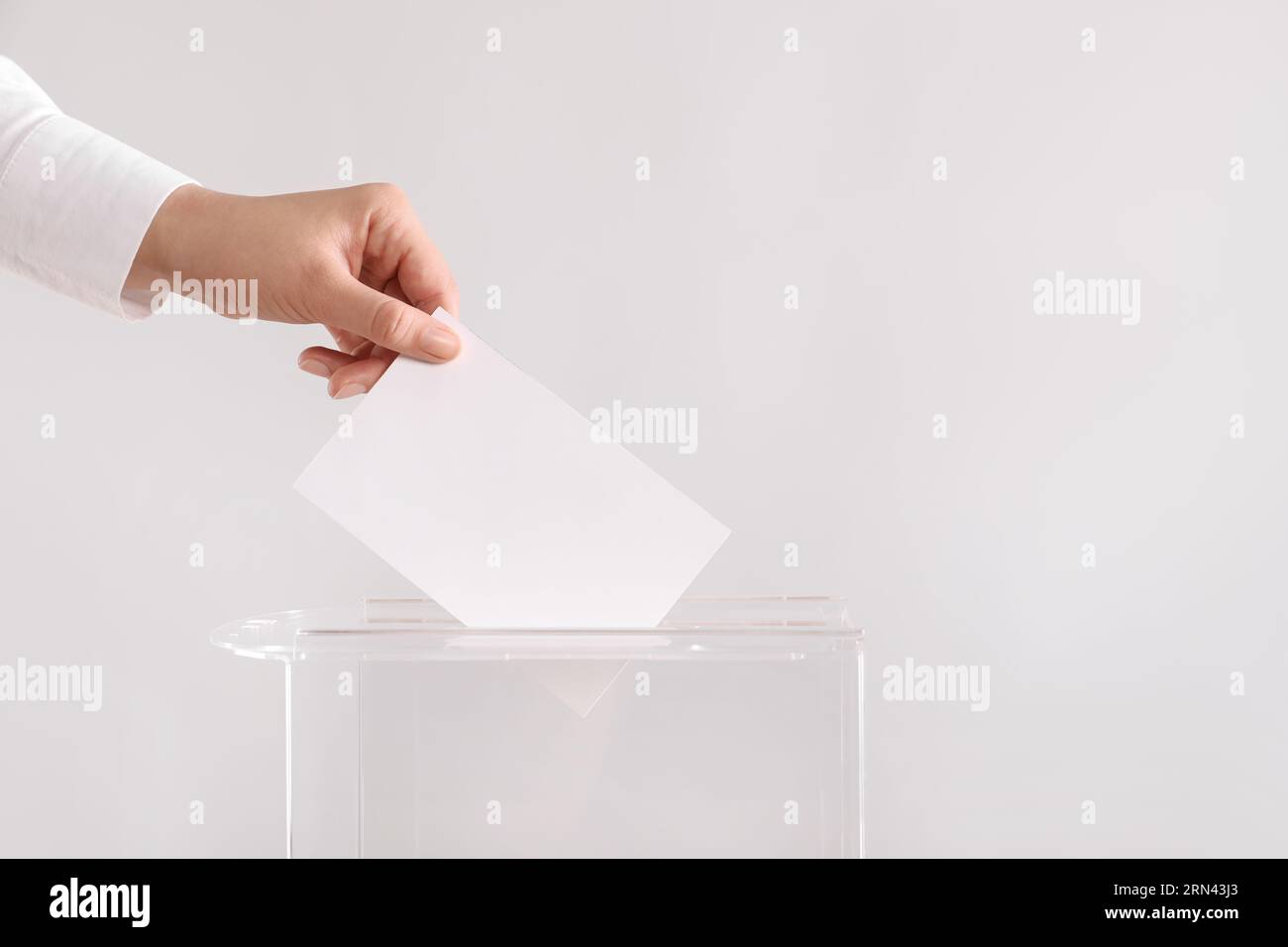 Woman putting her vote into ballot box on light grey background ...