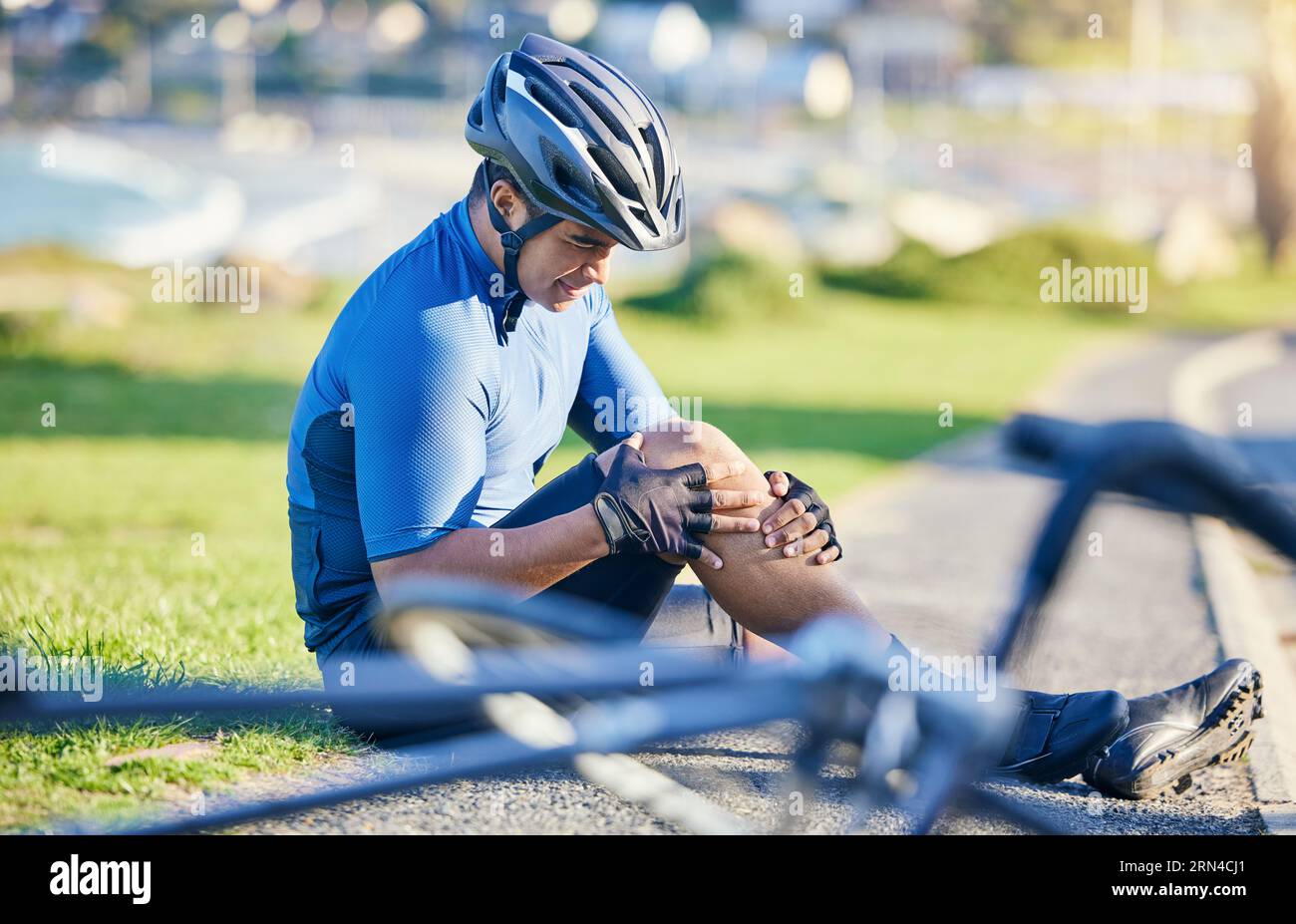 Man, outdoor and biker with knee pain, road and emergency with accident ...