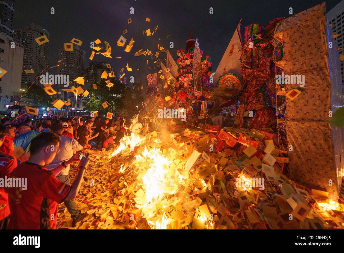 Ethnic Chinese throw paper offerings in-front of a giant paper statue ...
