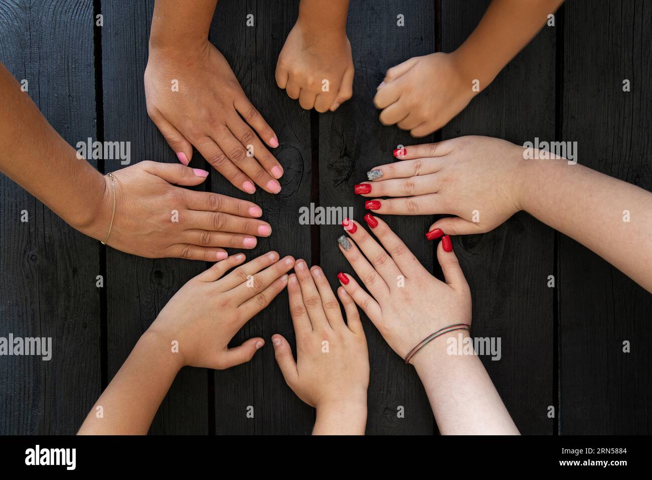 Female hands and child's hands on a wooden black board as a team, strength and unity of the ...