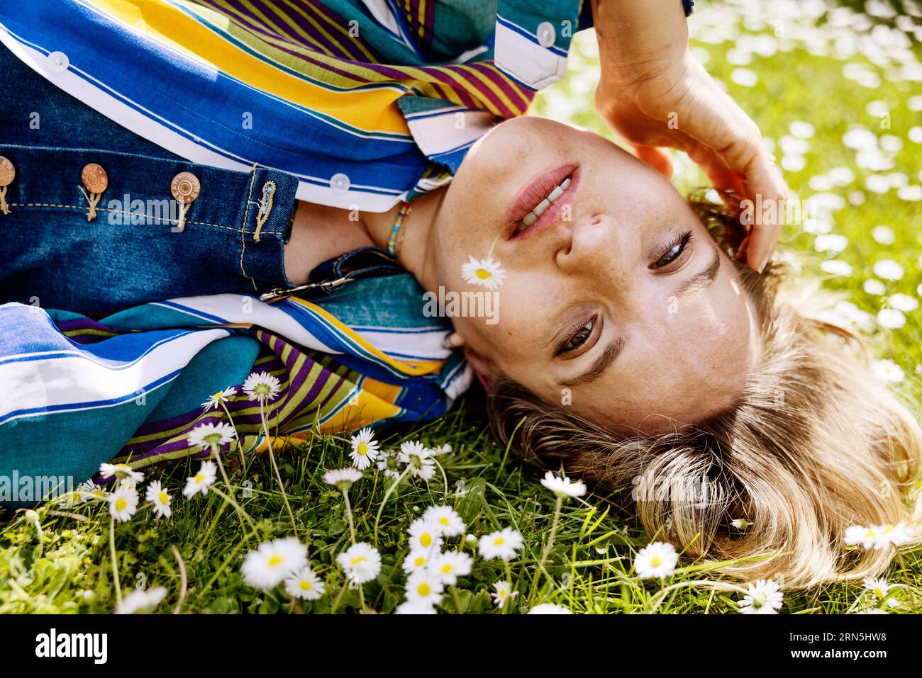 Pretty young woman lying in the grass between daisies with a daisy in ...