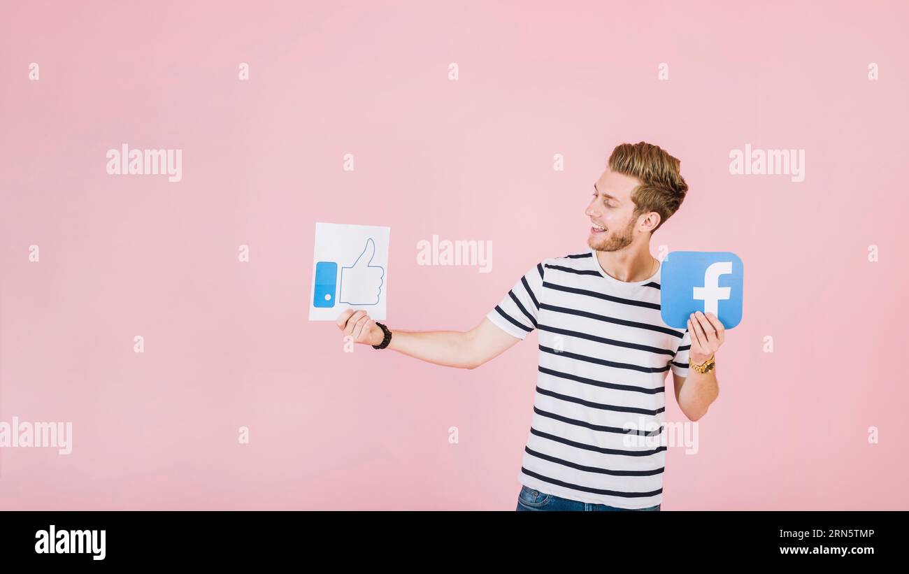 Smiling young man holding like facebook icon Stock Photo - Alamy