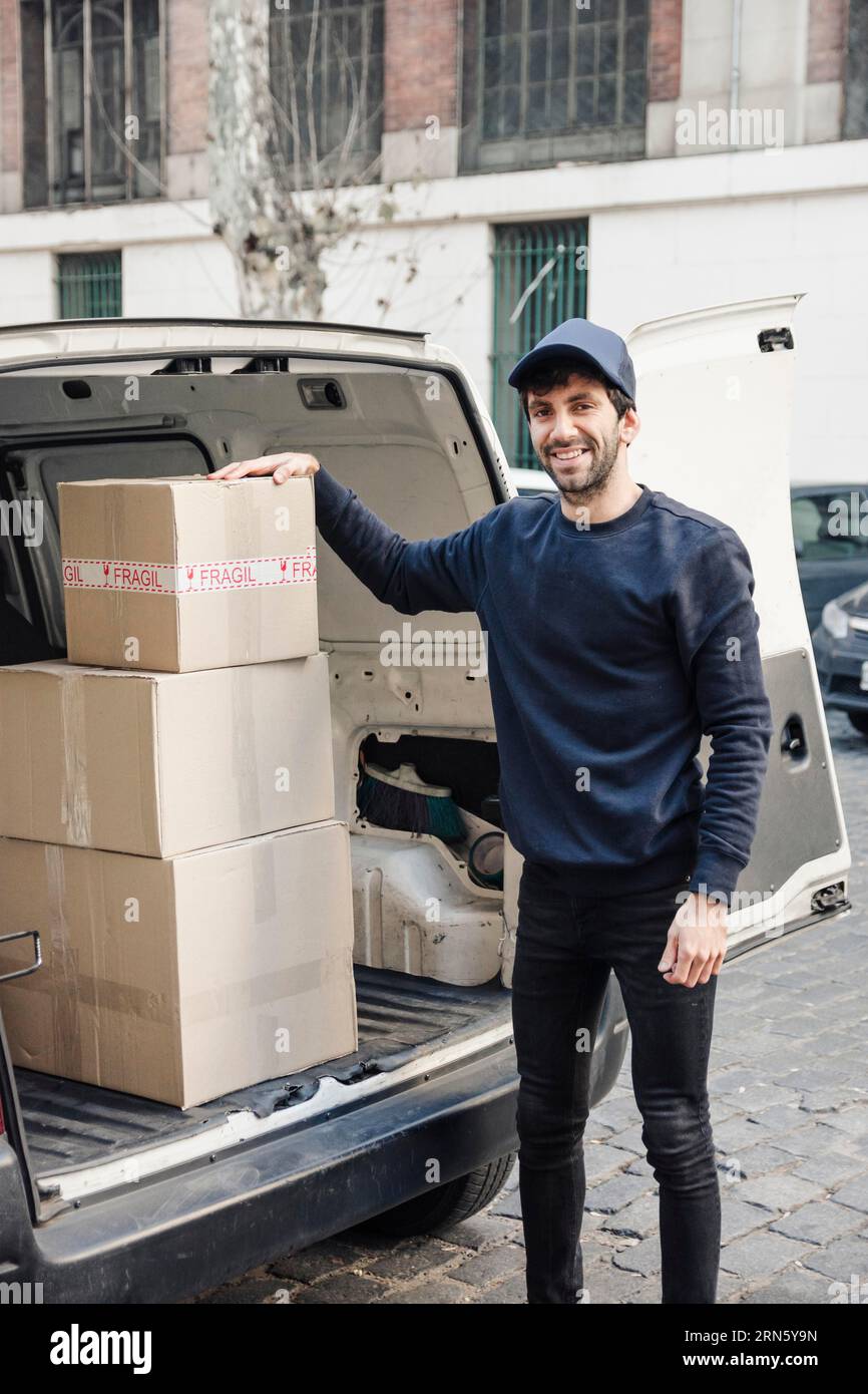 Portrait happy delivery man standing near vehicle with cardboard boxes ...