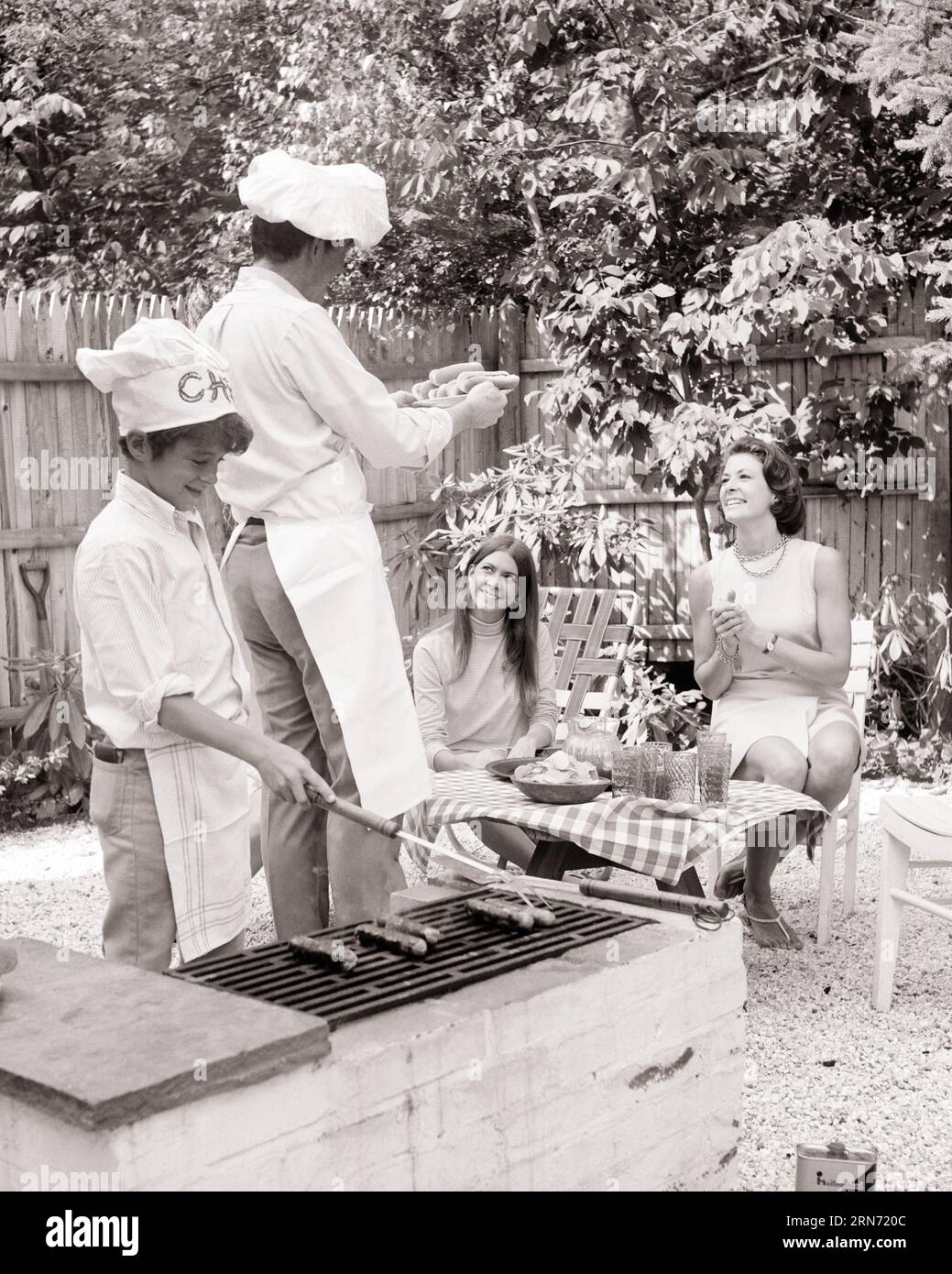 1960s FAMILY COOKING OUT IN BACKYARD SON AT GRILL FATHER SERVING MOTHER ...