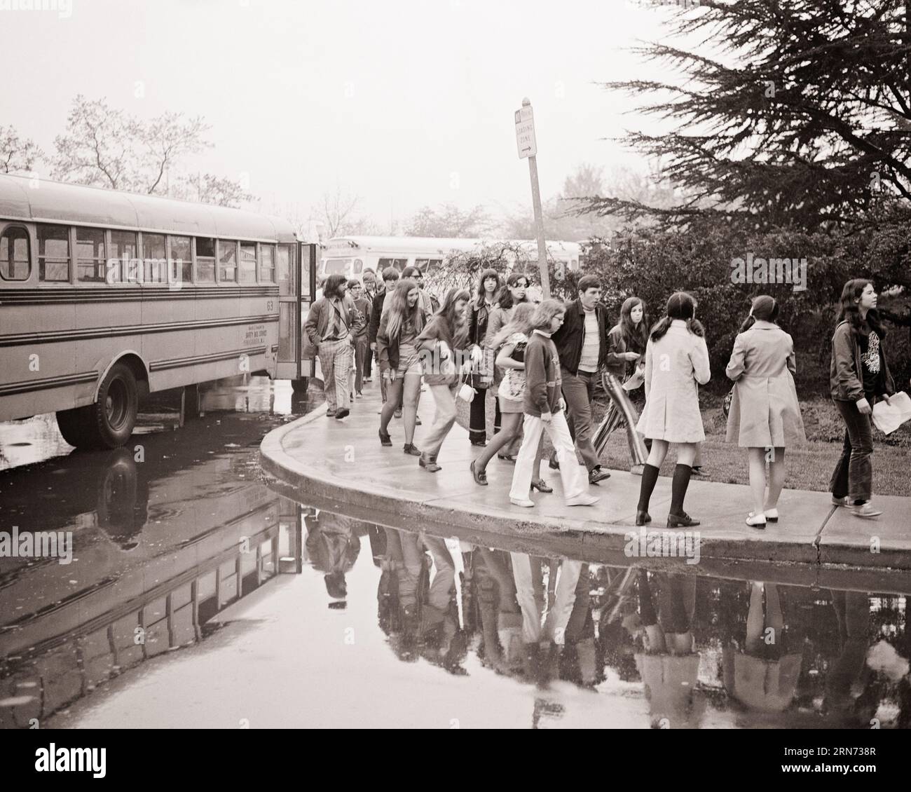 1970s GROUPS OF HIGH SCHOOL STUDENTS LEAVING SCHOOL BUSES ONTO A RAINY ...