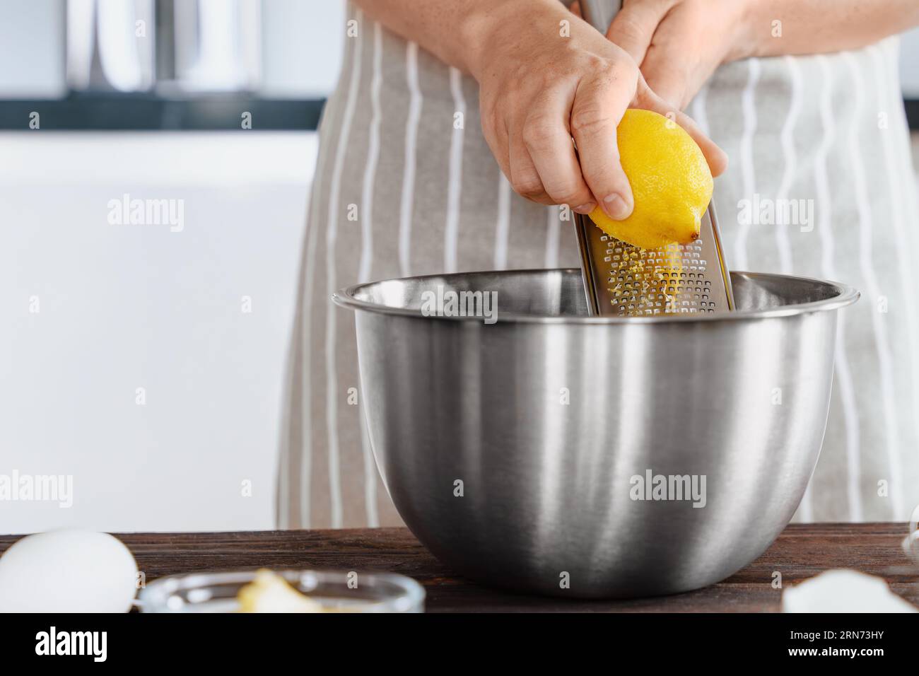 The cook's hands grate the zest of a lemon into a bowl of dough ...