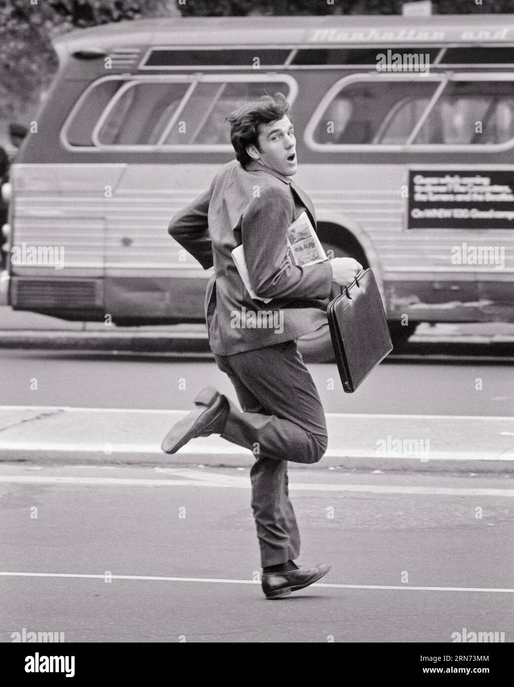 1970s YOUNG BUSINESSMAN RUNNING TO CATCH MORNING BUS WITH BRIEFCASE AND ...