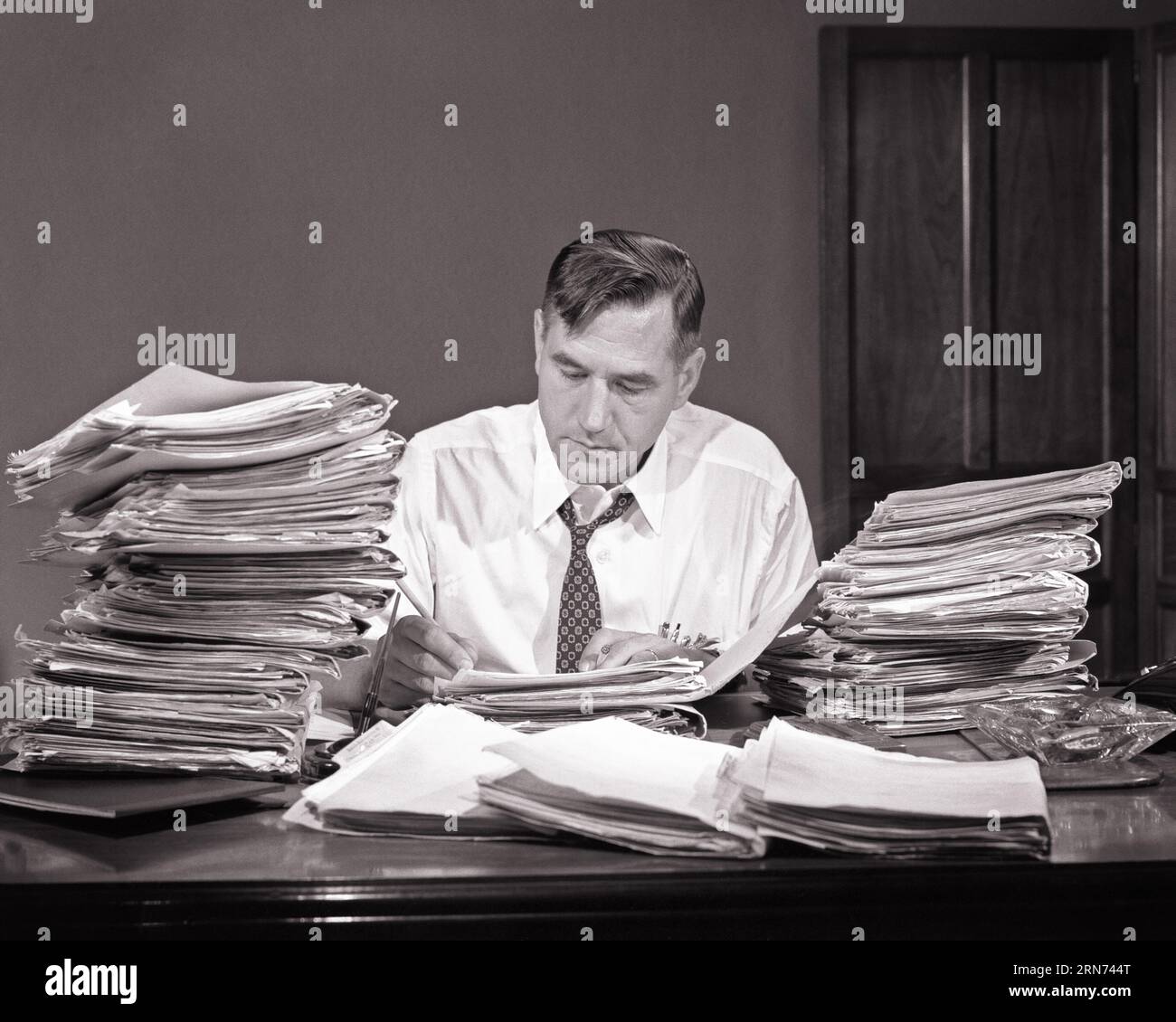 1953 1950s MAN SITTING AT OFFICE DESK LOOKING DOWN WRITING READING ...
