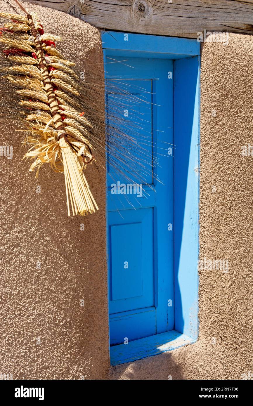 Decorative sheaf of wheat hang from wooden lintel over blue shuttered ...