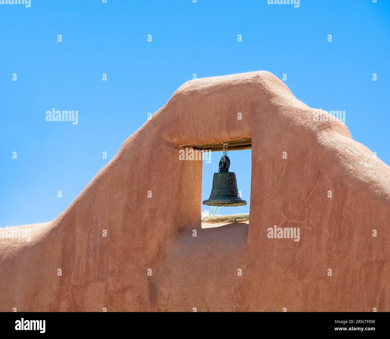 Weathered cast iron bell hangs on adobe bell gable structure set ...