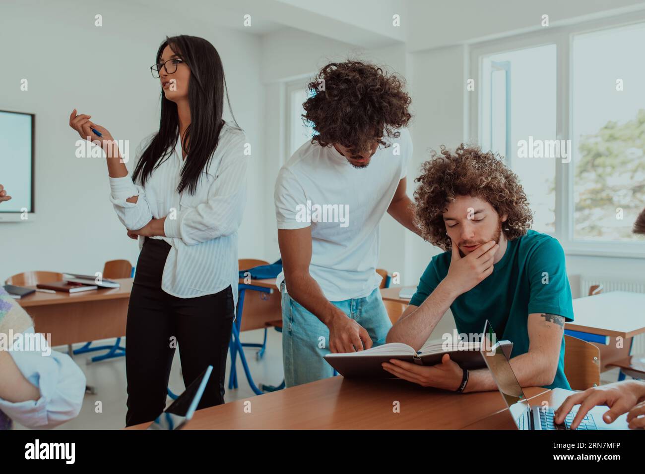 A diverse group of students gathers in a modern school classroom ...