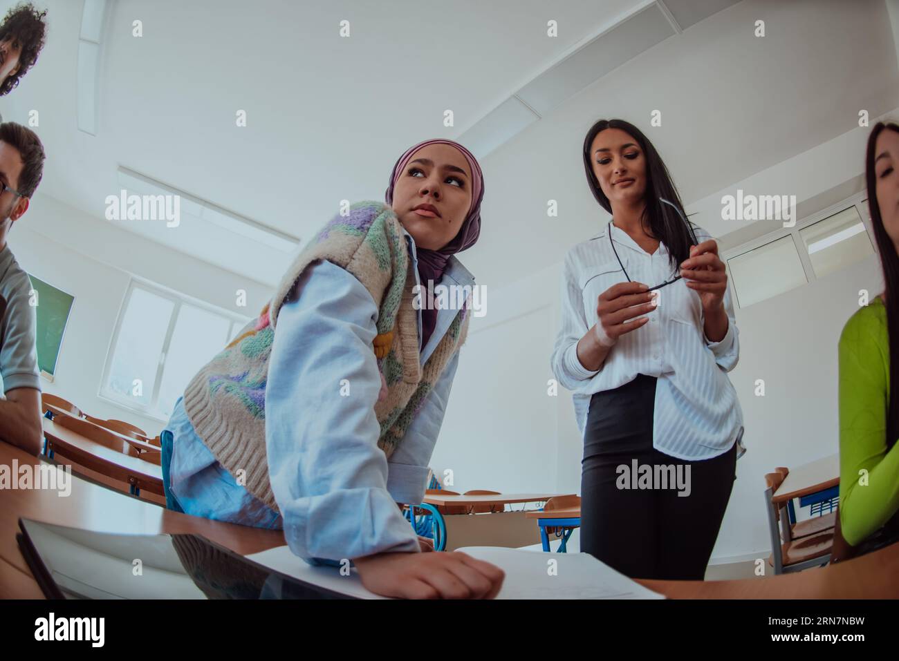 A diverse group of students gathers in a modern school classroom ...
