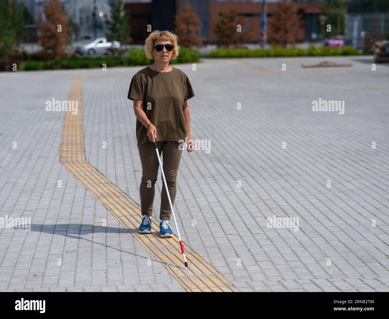 An elderly blind woman walks with a cane along a tactile tile Stock ...
