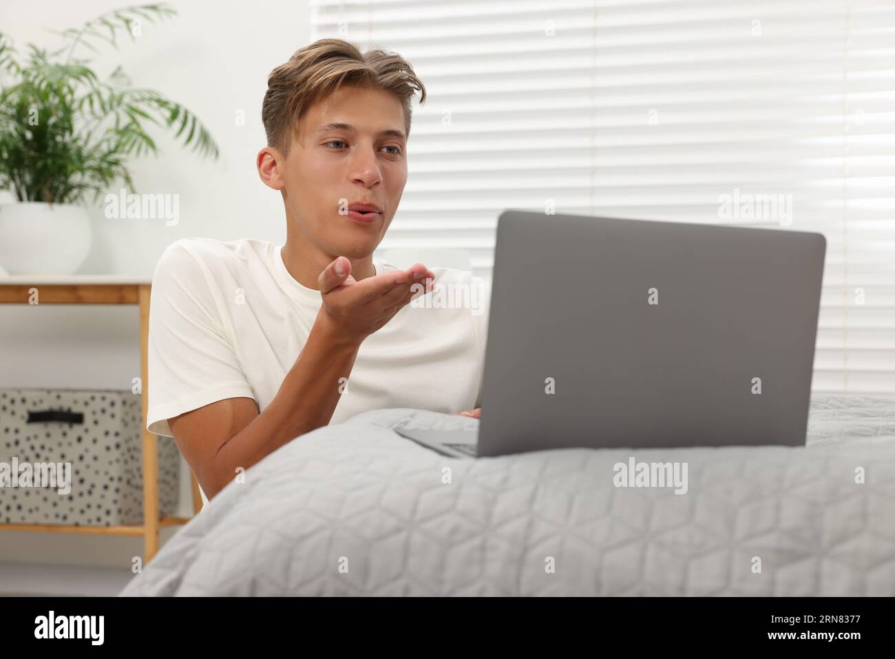 Happy young man having video chat via laptop and blowing kiss on bed ...