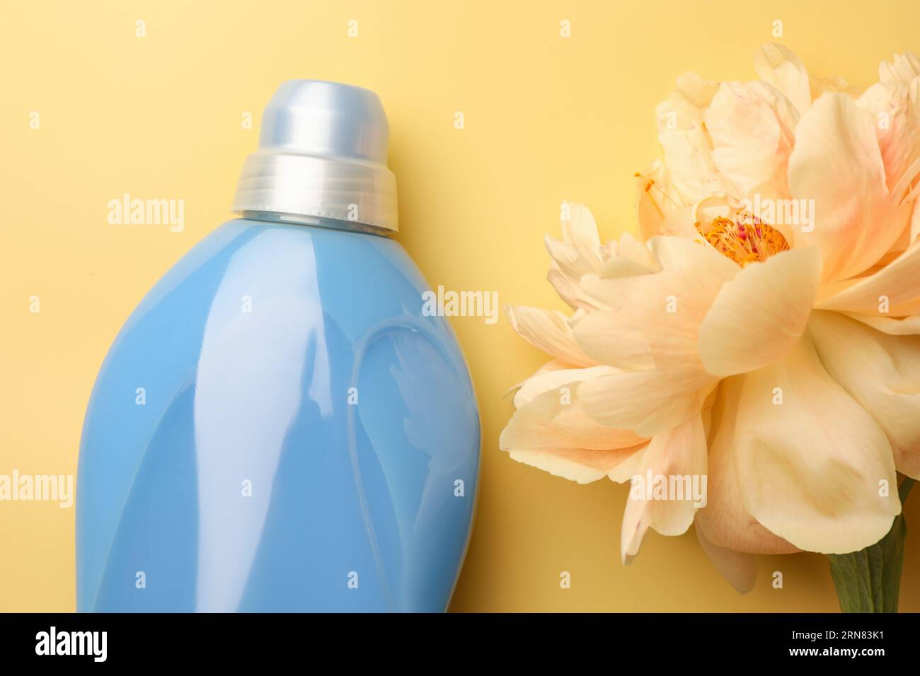 Bottle of fabric softener and beautiful peony flower on pale yellow ...