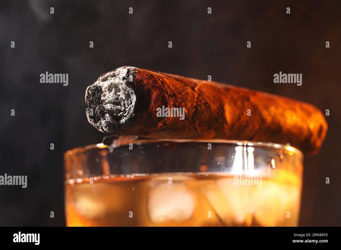 Glass of whiskey with ice cubes and smoldering cigar against black ...