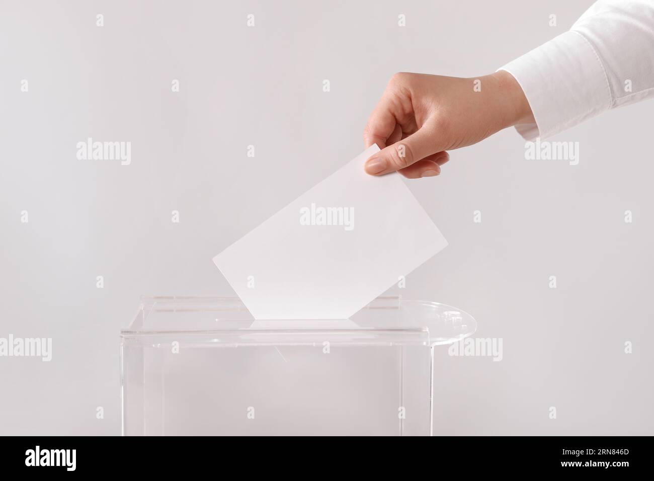 Woman putting her vote into ballot box on light grey background ...