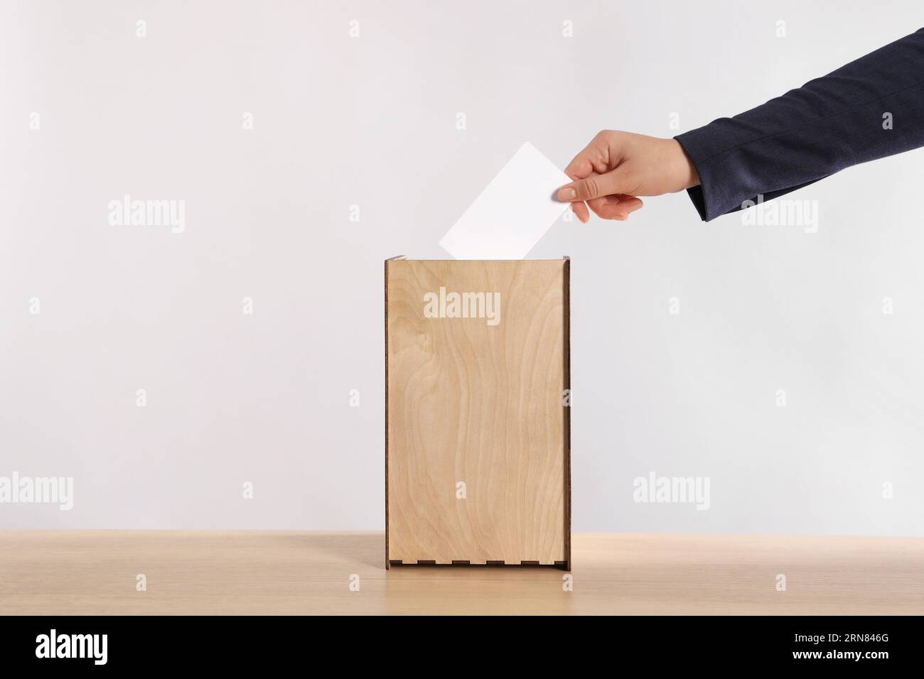 Woman putting her vote into ballot box on wooden table against light ...