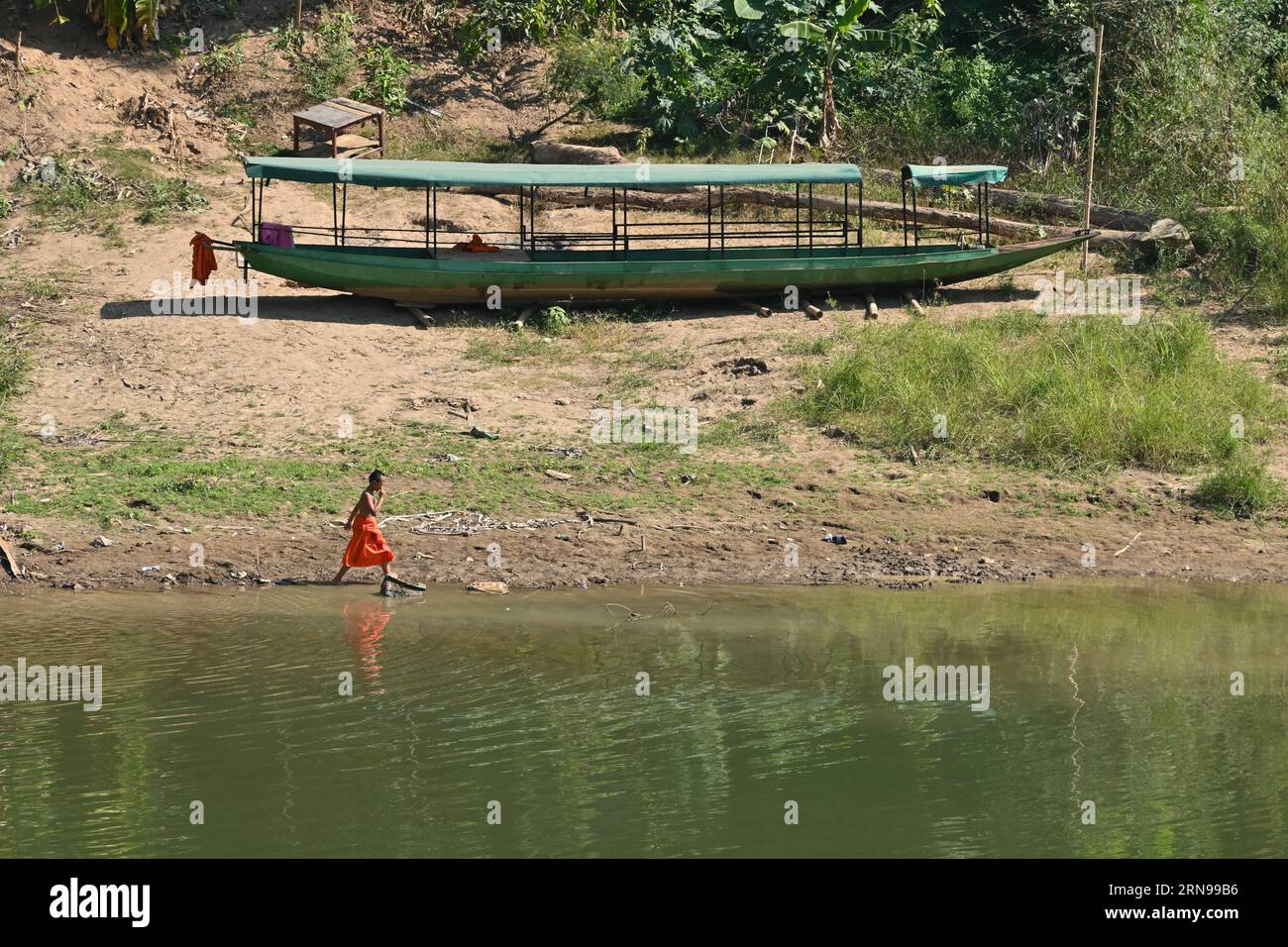 Young buddhist monk taking bath in the river near a boat in Luang ...