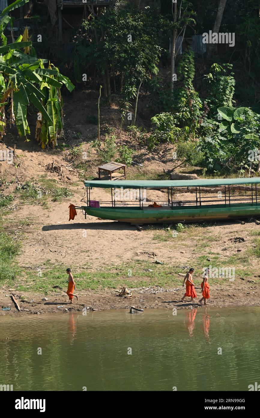 Young buddhist monk taking bath in the river near a boat in Luang ...