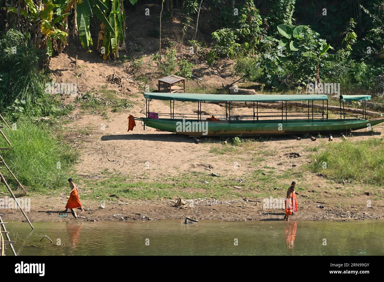 Young buddhist monk taking bath in the river near a boat in Luang ...