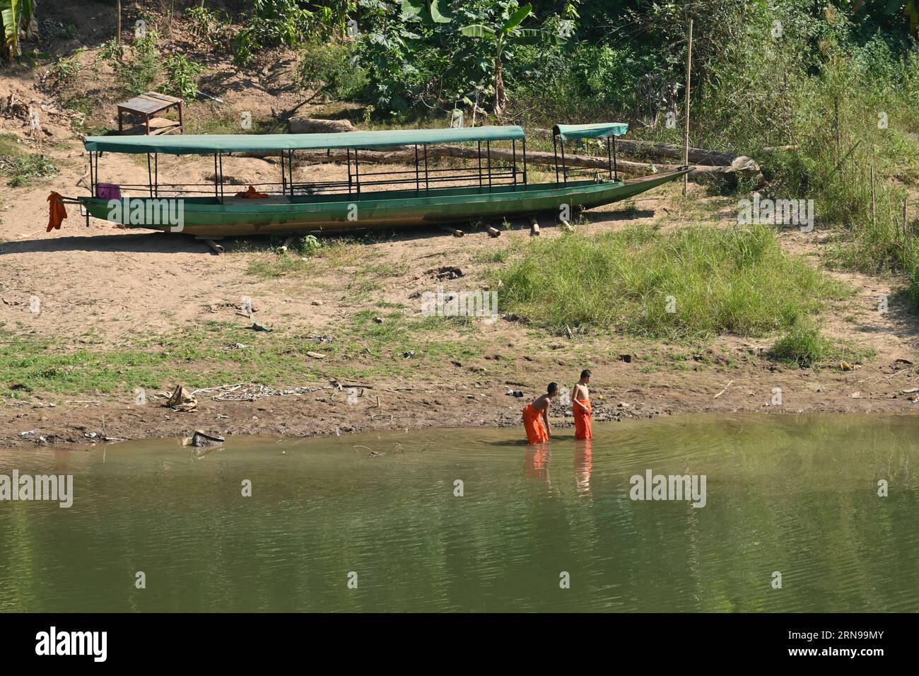 Young buddhist monk taking bath in the river near a boat in Luang ...