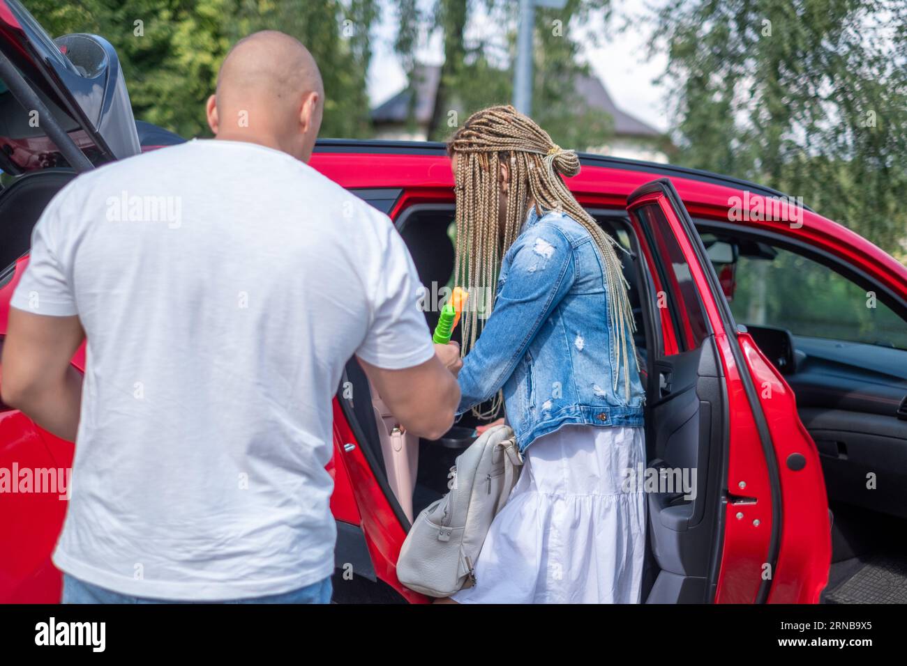 Woman and a man take things from a red car and get ready for a trip ...